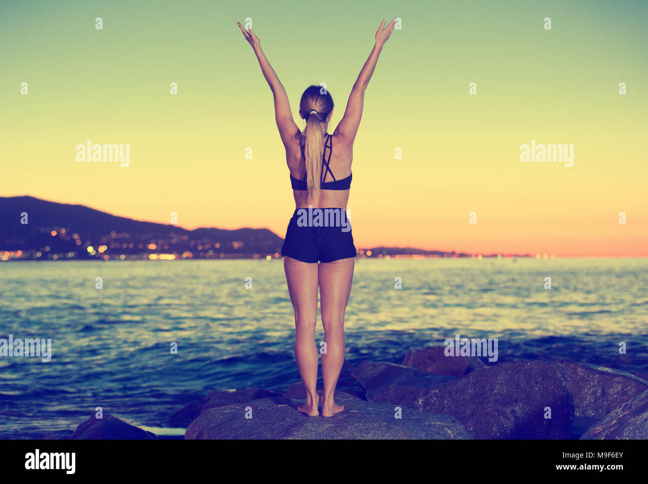 Adult woman is practicing stretching on a rock near sea at the dawn ...