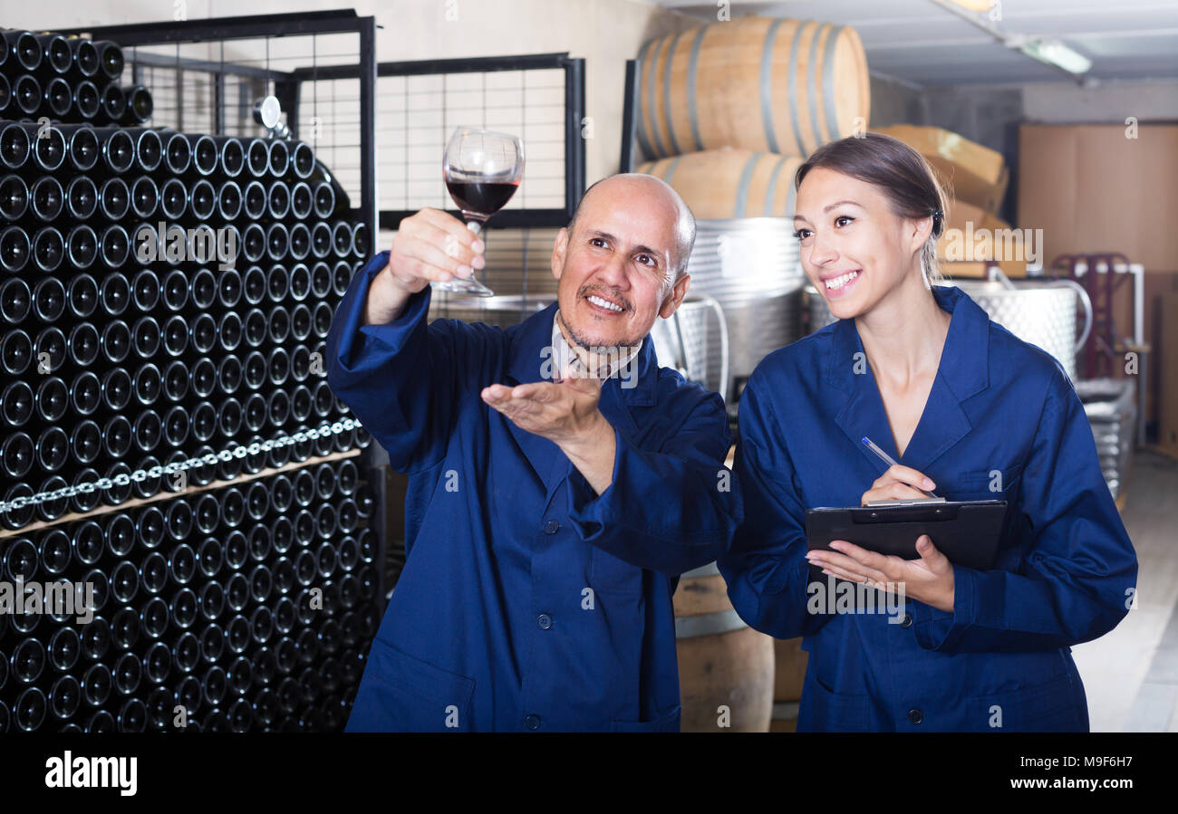 Glad girl with cardboard standing with male worker in small winery ...
