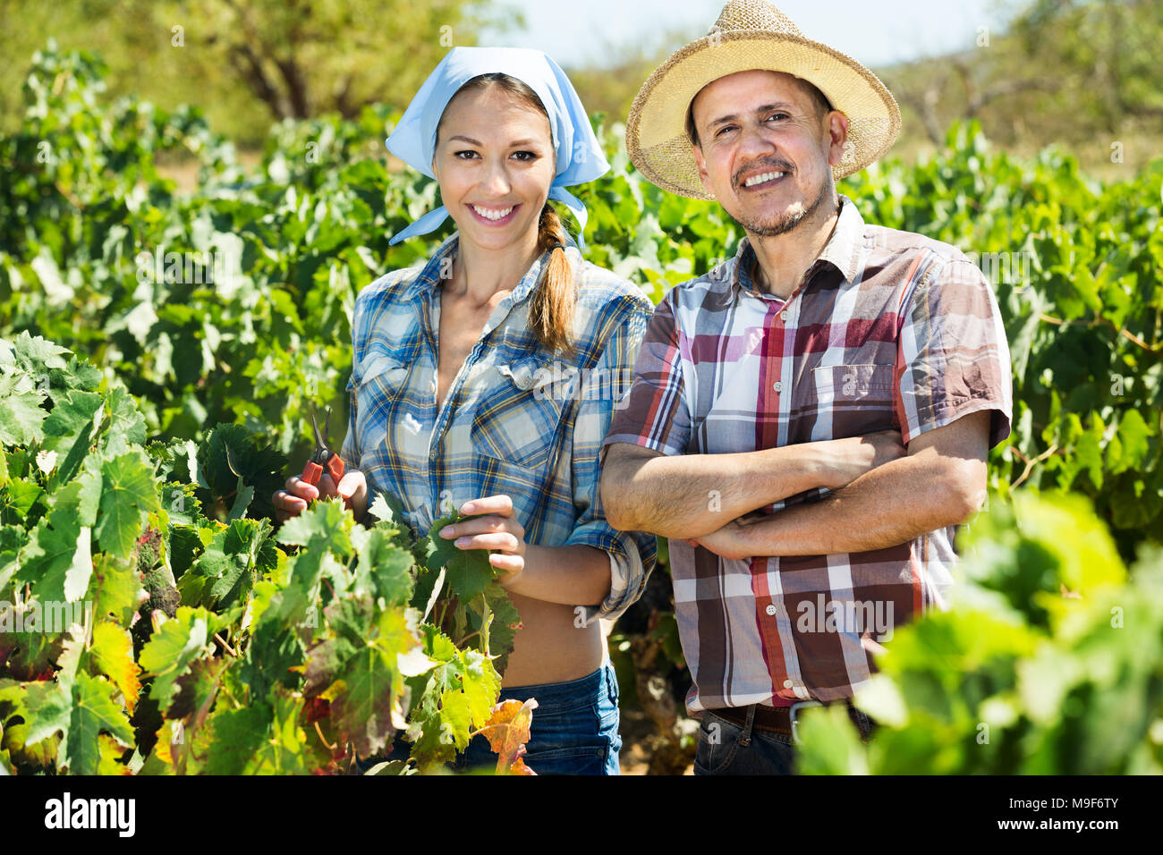 Two cheerful smiling gardeners standing together in grapes tree yard ...