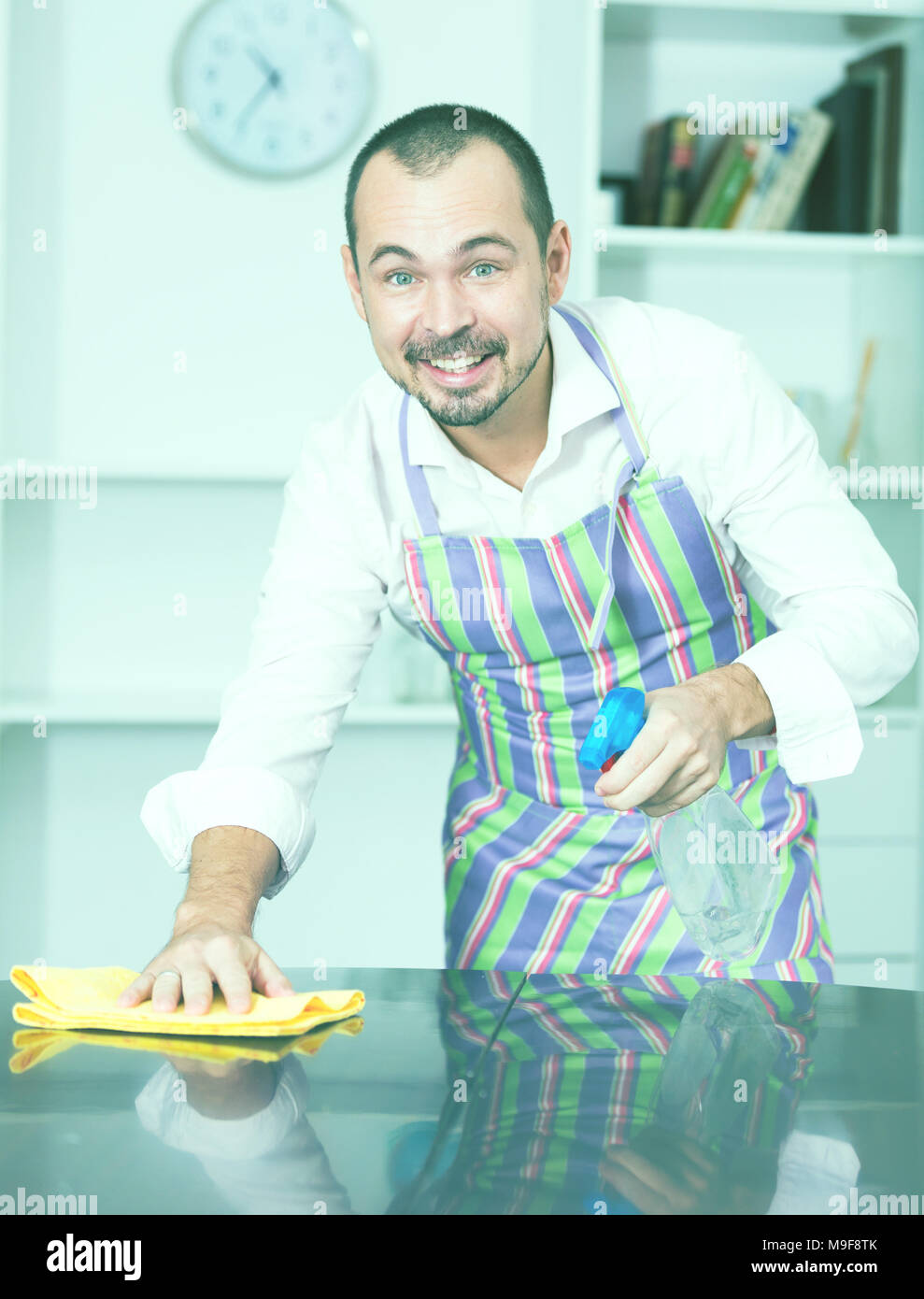Positive young man in apron cleaning his office desk by cleanser Stock ...