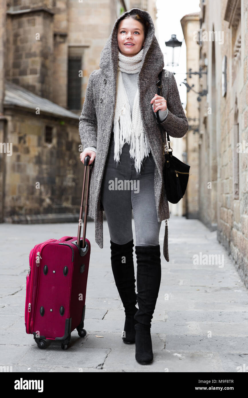 positive young girl in hood and coat with baggage in autumn season ...