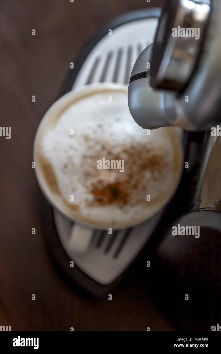 White cup standing on the grating of coffee machine with coffee pouring ...