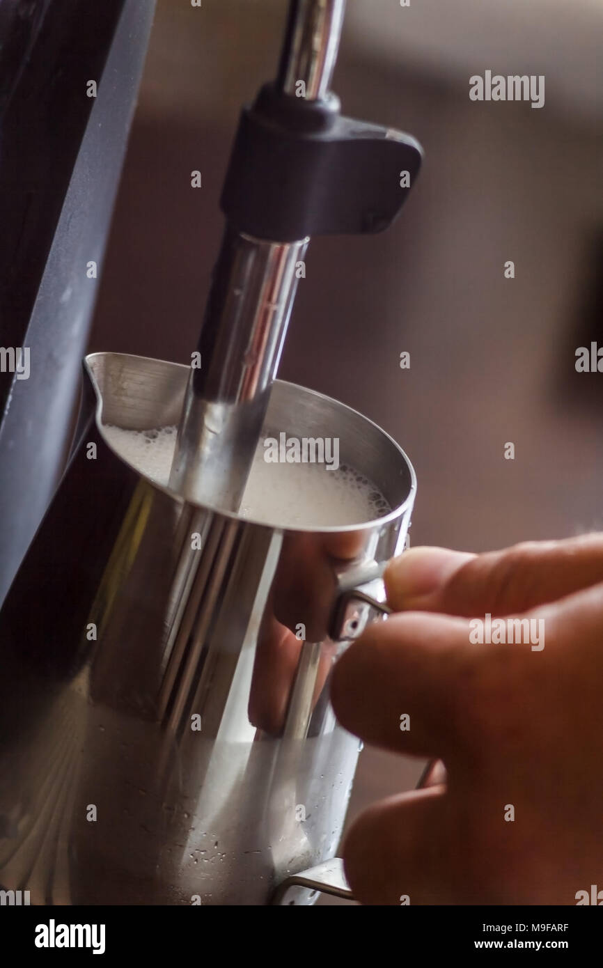 Professional bartender warming milk for cappuccino. Barista using coffee machine for latte art ...