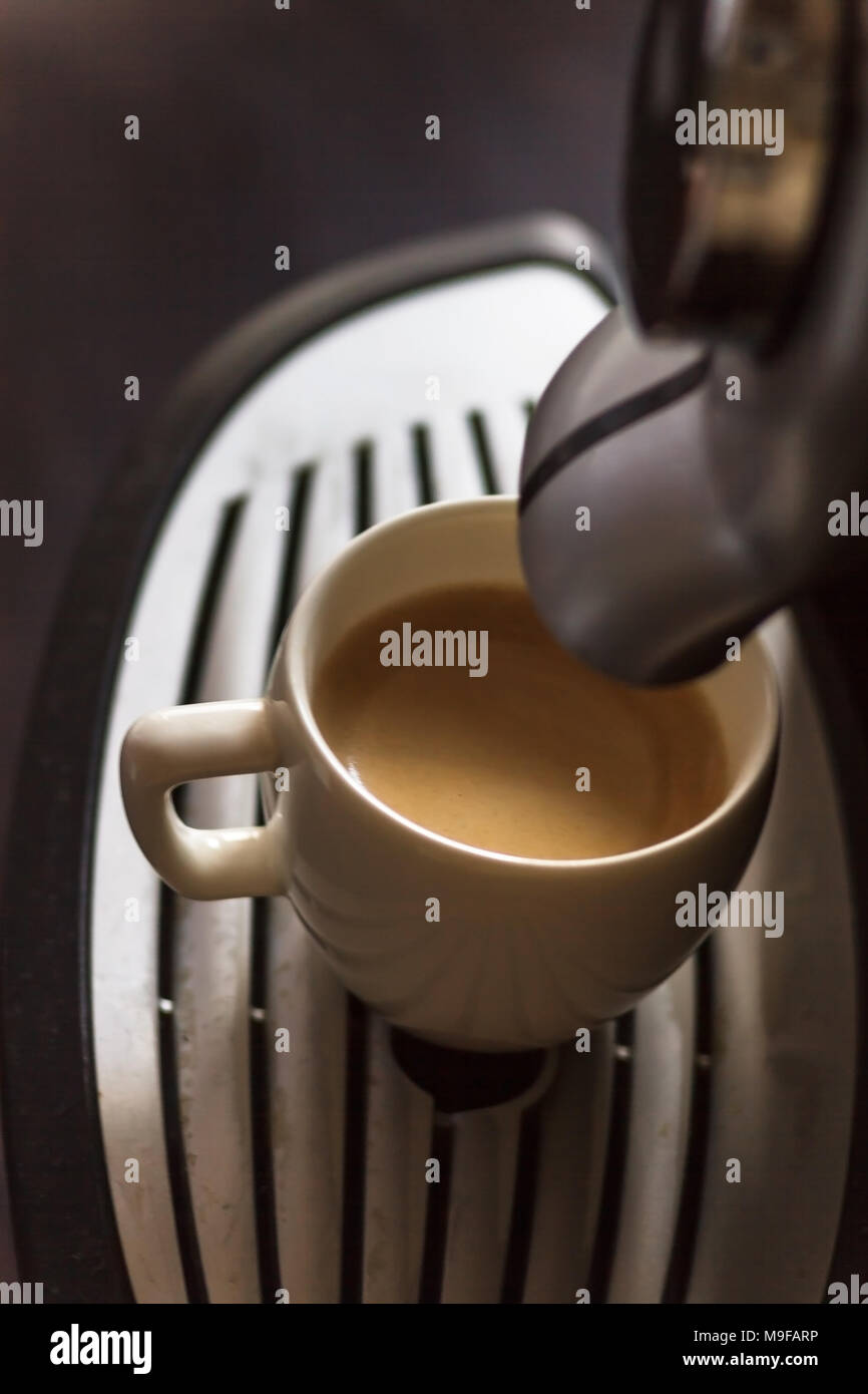 White cup standing on the grating of coffee machine with coffee pouring ...
