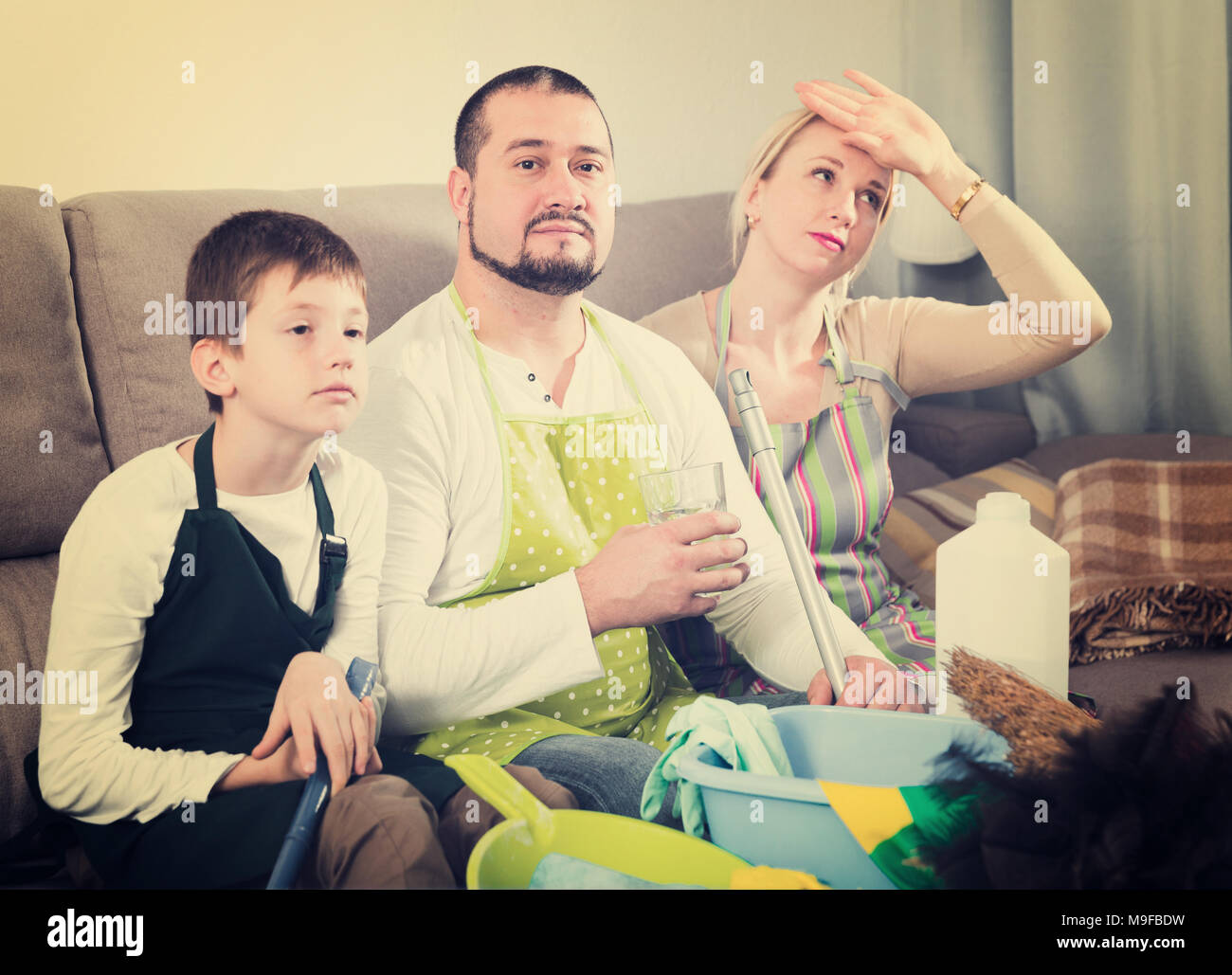 Tired friendly family sitting on sofa after home cleaning Stock Photo ...