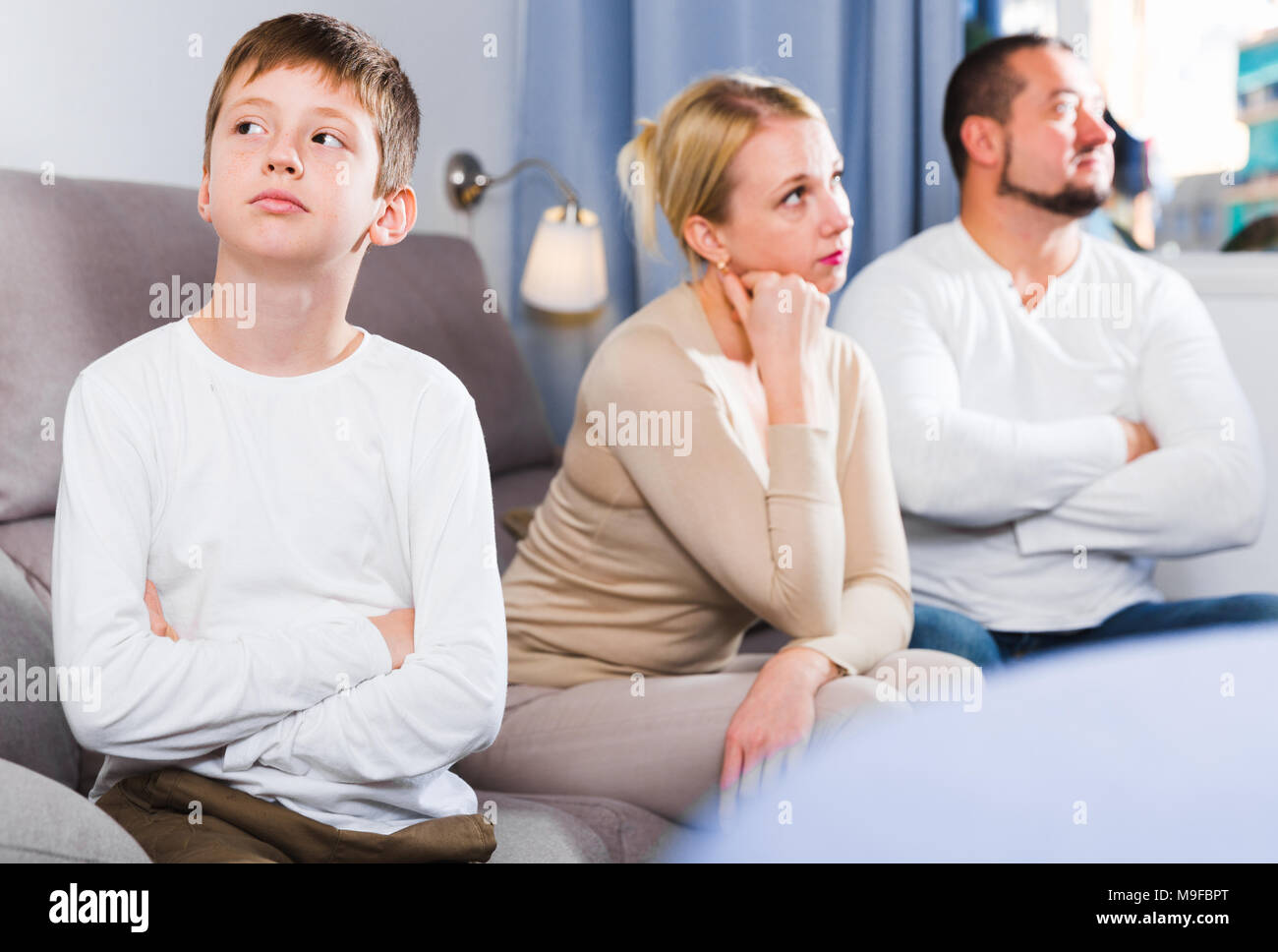 Upset son and frustrated parents sitting on sofa and looking away after ...
