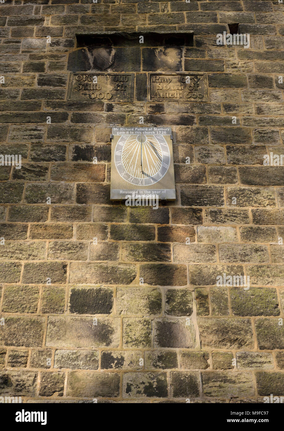 Vertical wall mounted sundial on church wall with dappled sunlight and ...