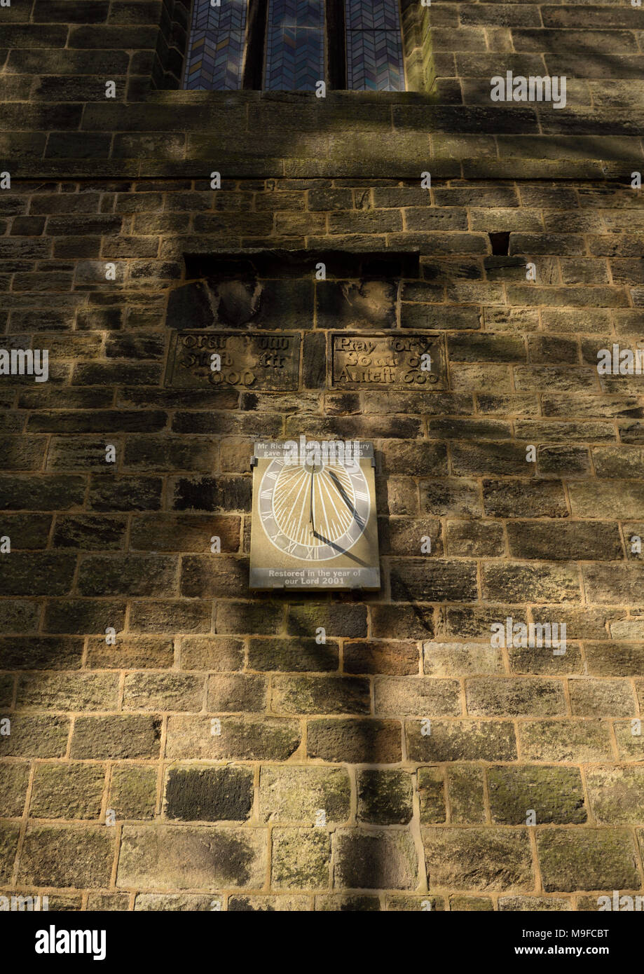 Vertical wall mounted sundial on church wall with dappled sunlight and ...