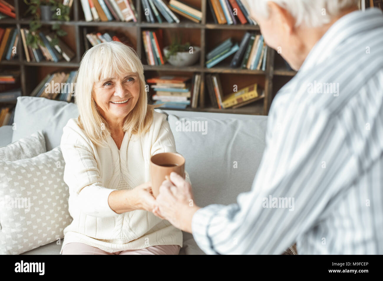 Aged man giving tea to a woman together at home in the living room ...