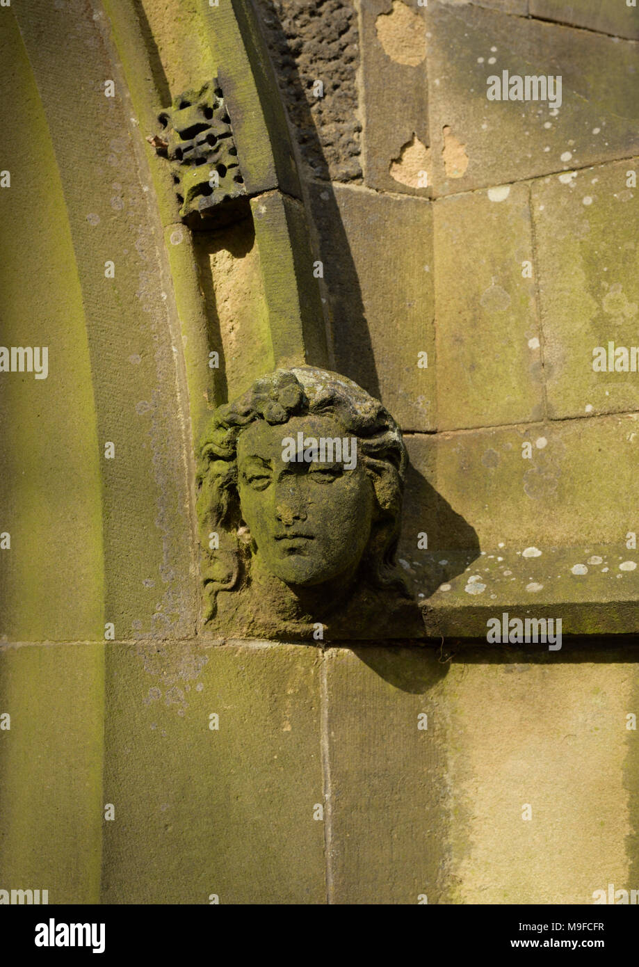 Damaged carved stone head label stop on base of arch with light ...