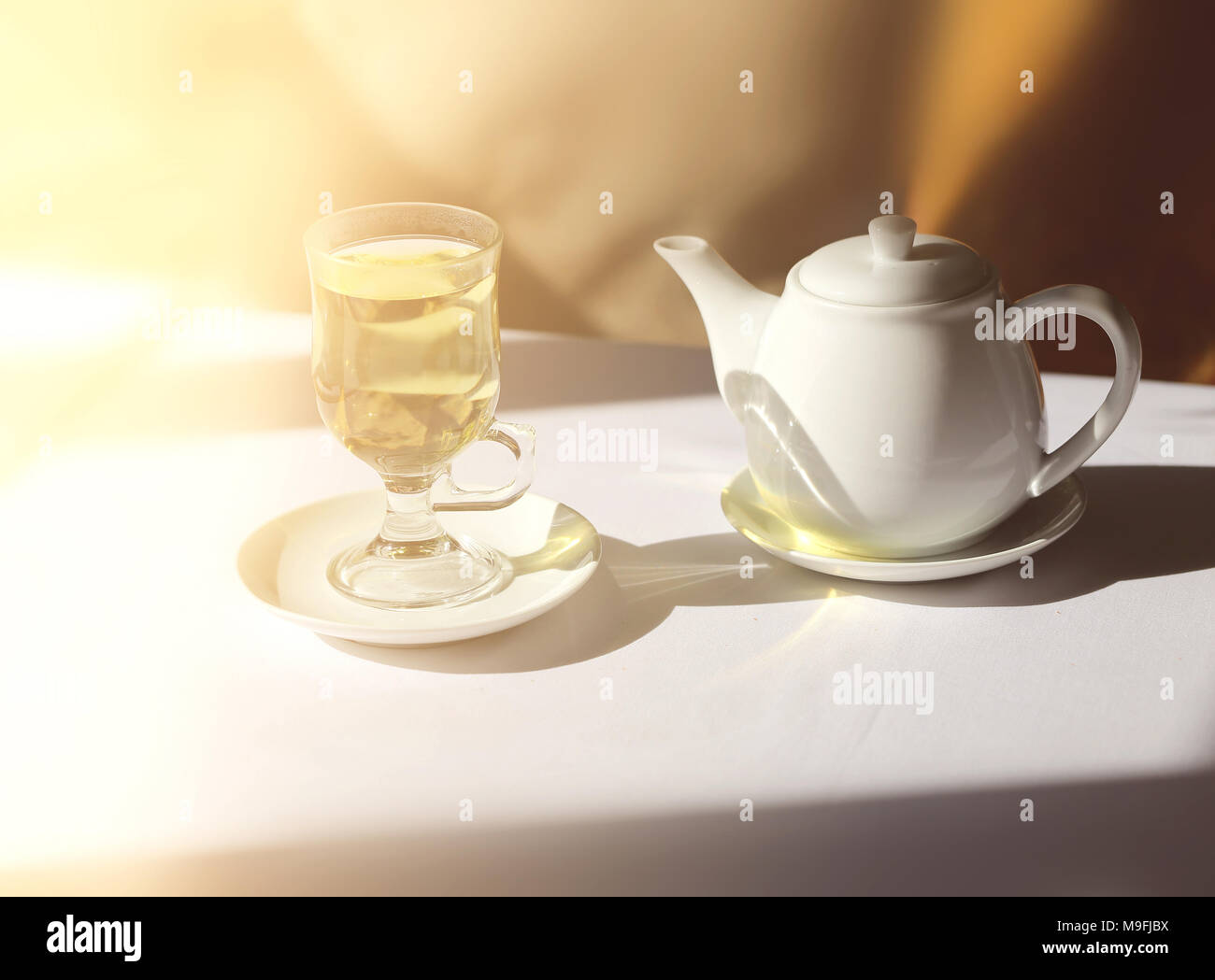 Retro photo of a glass of tea and a kettle on a table lit by the sun ...