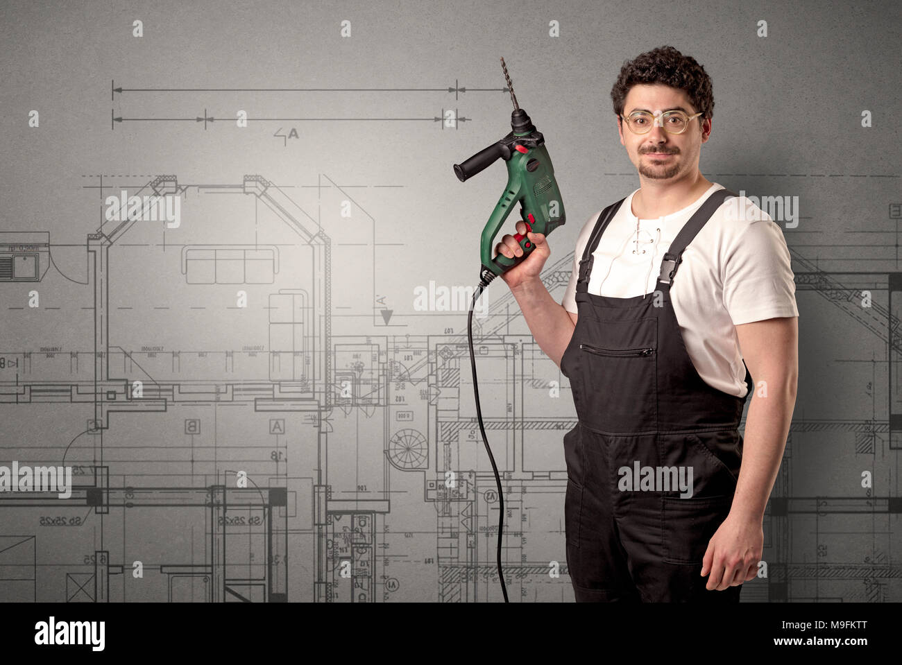Worker standing with tool in his hand in front of technical drawings ...