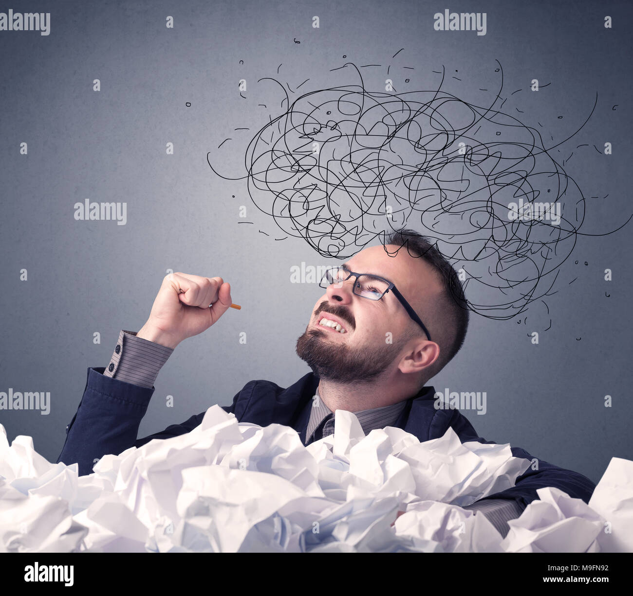 Young businessman sitting behind crumpled paper with scribbles over his ...