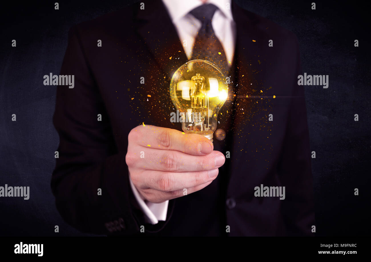An elegant office worker holding a yellow sparkling light bulb in his ...