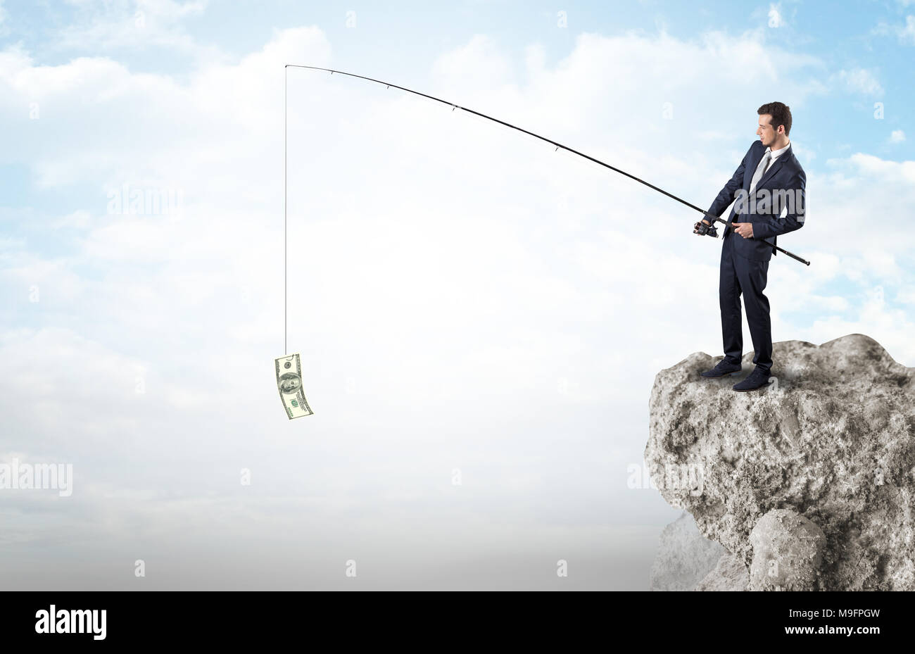 Elegant young businessman fishing cash from a huge rock Stock Photo - Alamy