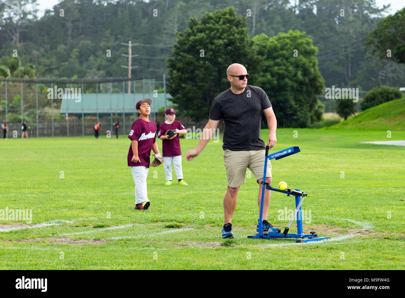 A adult uses a pitching machine following though with pitching arm ...