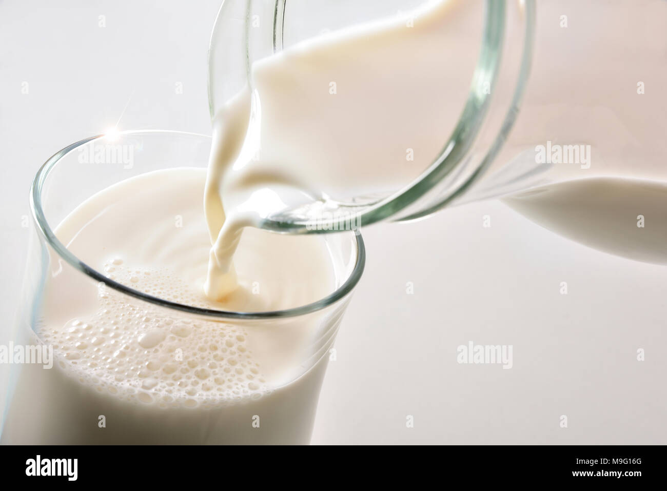 Filling glass of milk with a glass jug on white isolated background ...