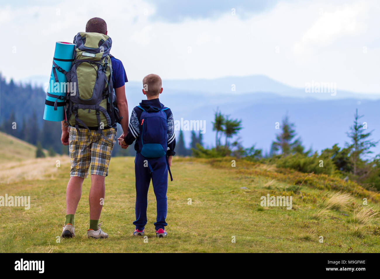 Father and son with backpacks hiking together in scenic summer green ...