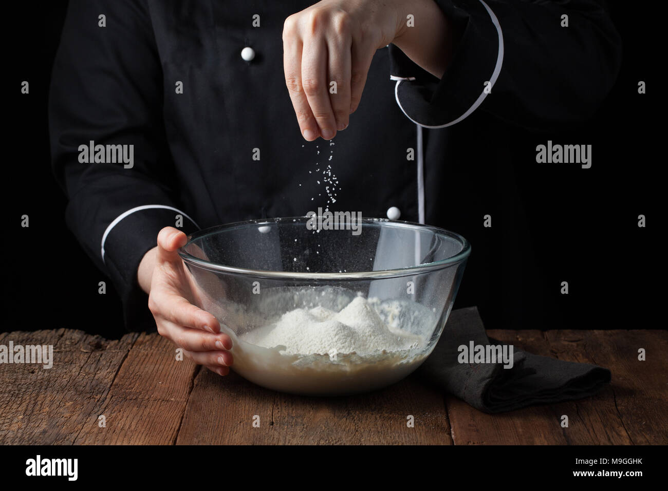 Chef hands sprinkles sea salt on raw dough on a black background ...