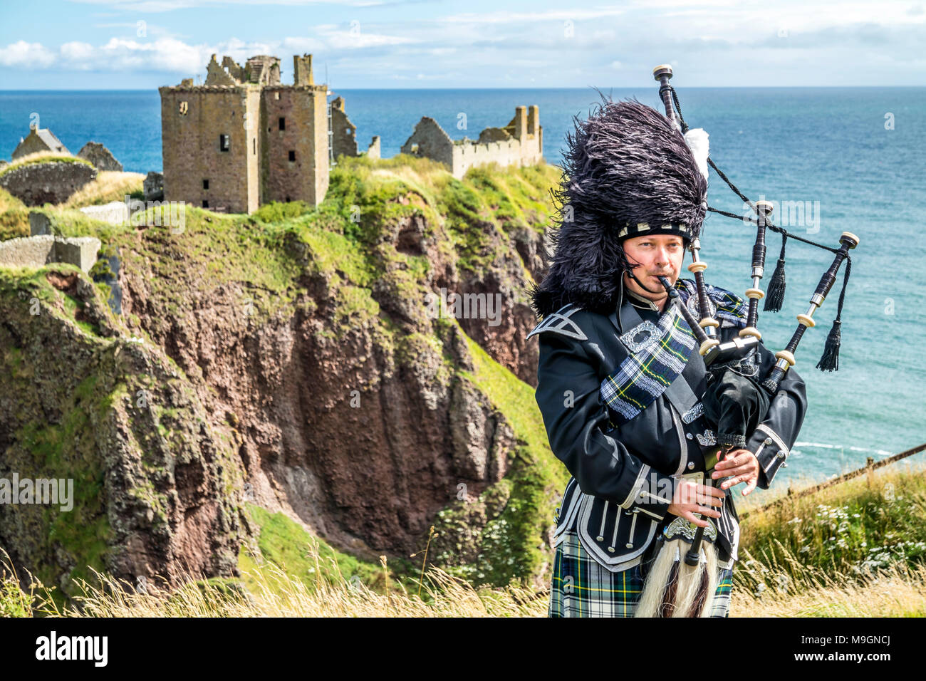 Traditional scottish bagpiper in full dress code at Dunnottar Castle in ...