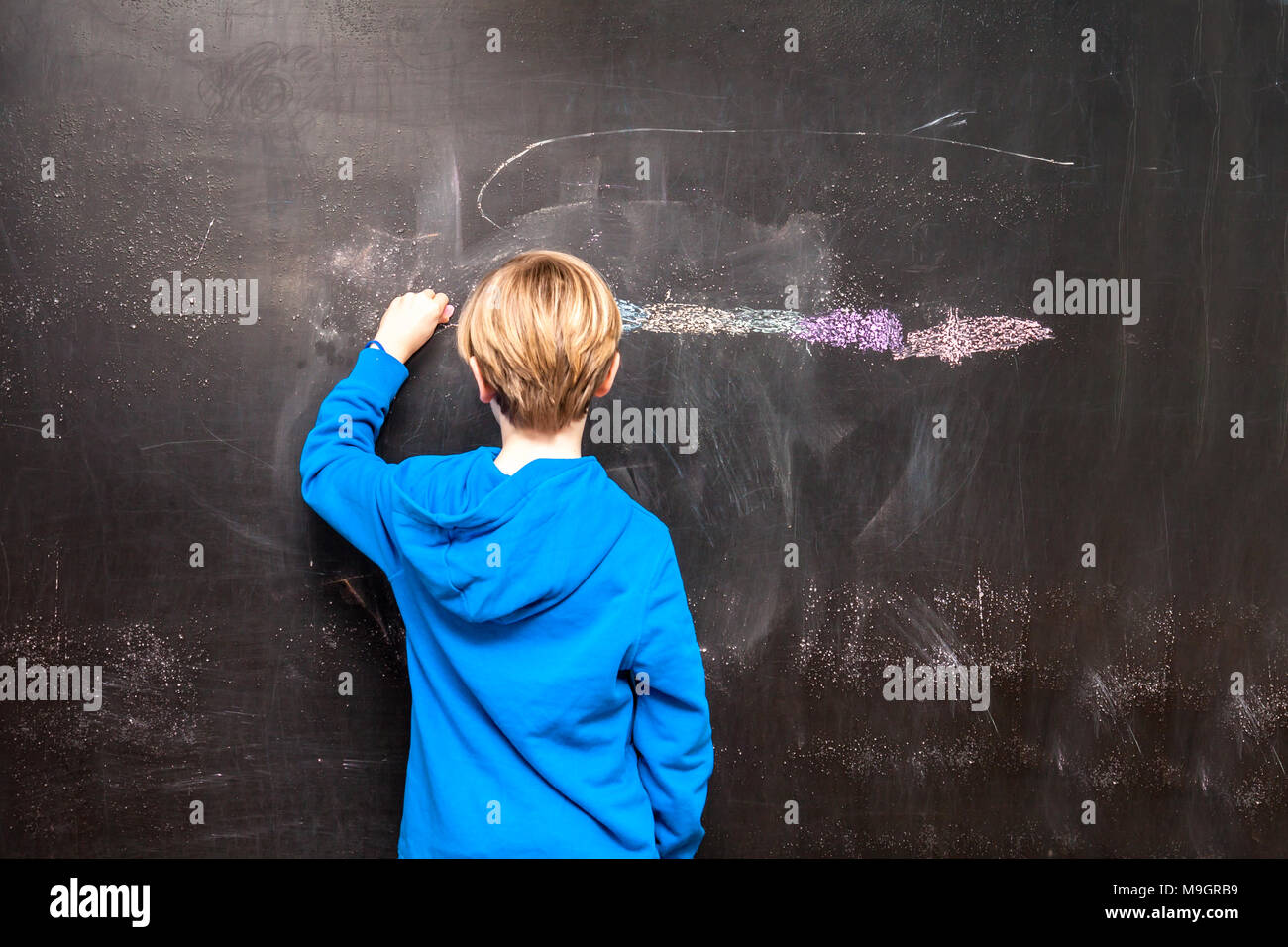 Back view of a little boy painting something on a chalkboard Stock ...