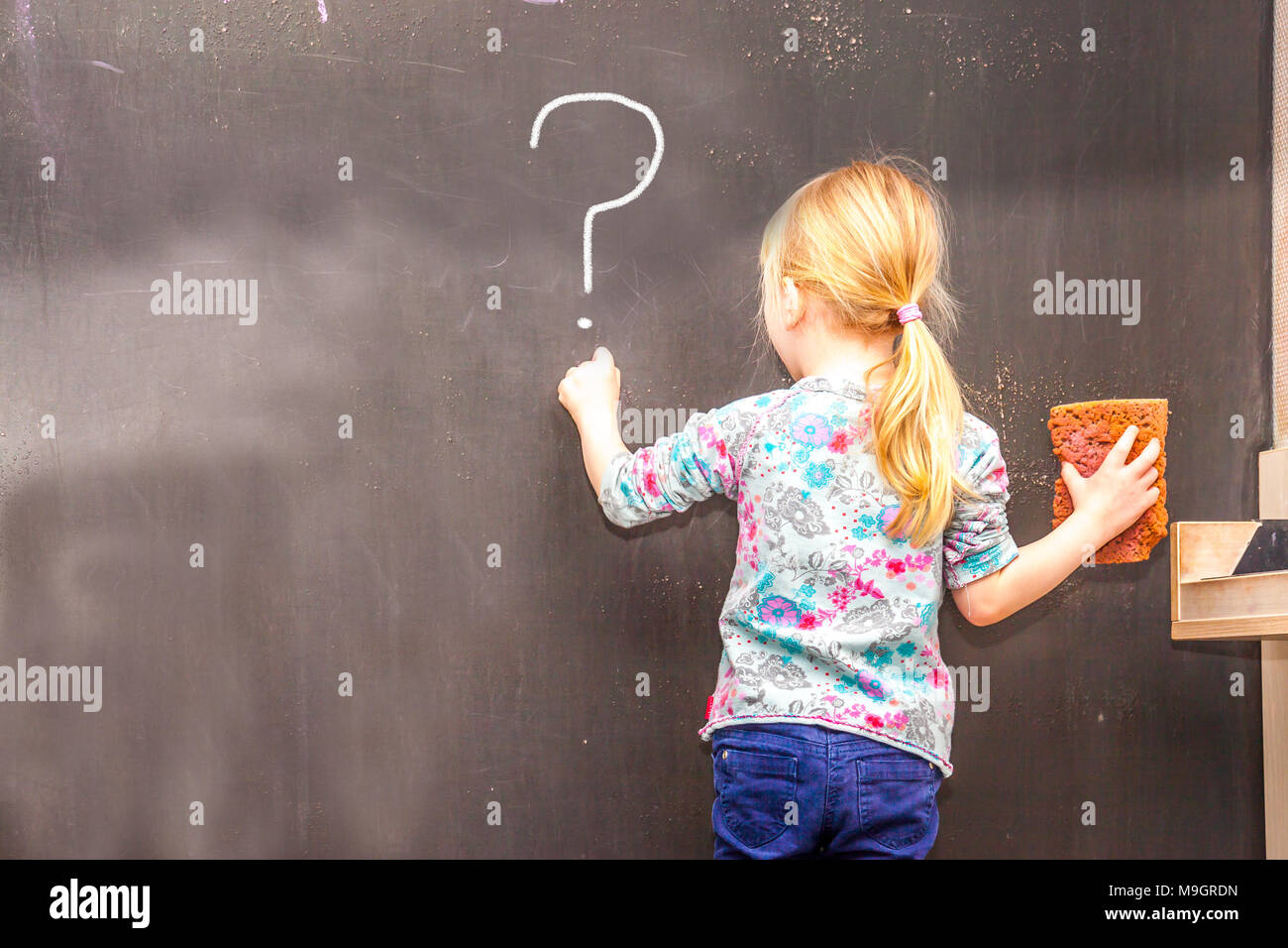 Cute little girl writing question mark on chalkboard in a classroom ...
