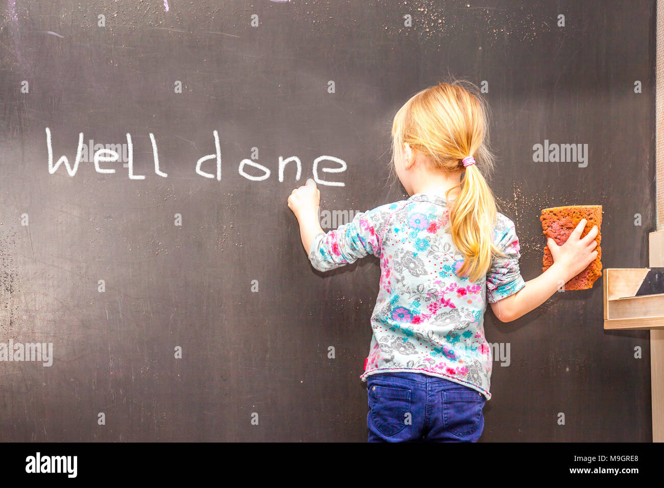 Cute little girl writing Well done on chalkboard in a classroom Stock ...