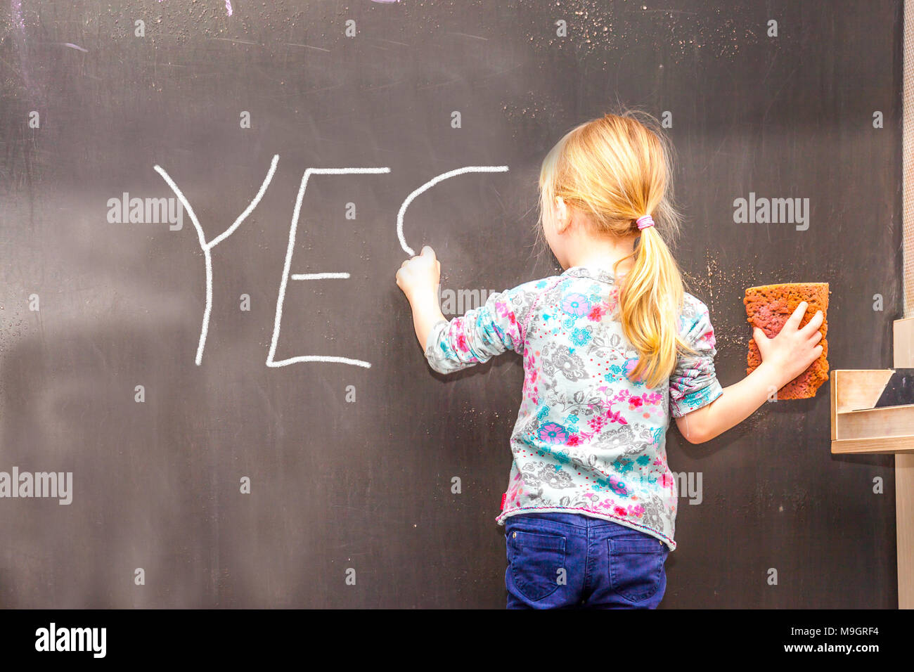 Cute little girl writing yes on chalkboard in a classroom Stock Photo ...