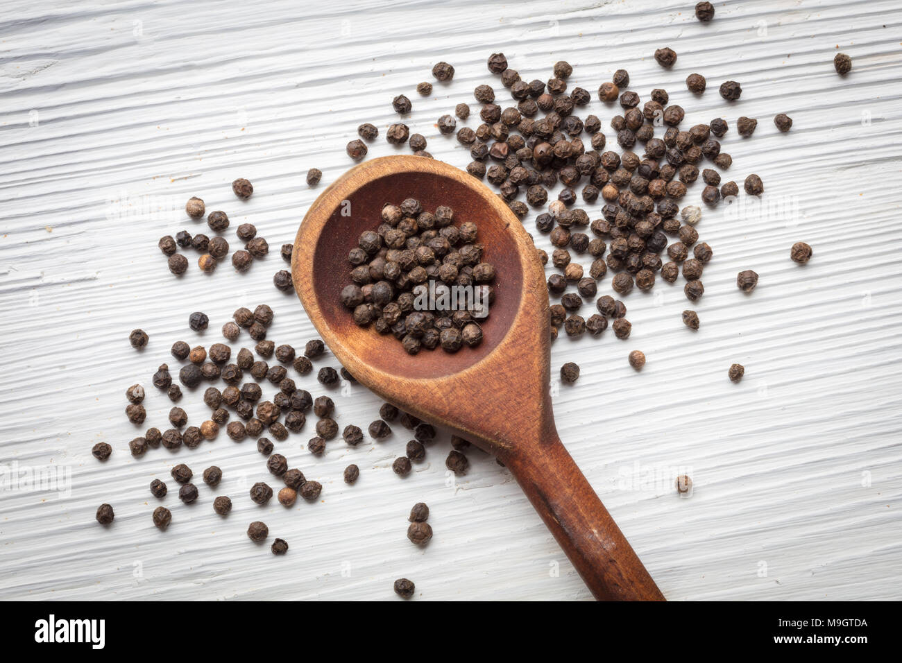 Black pepper corns on a white wooden background Stock Photo - Alamy