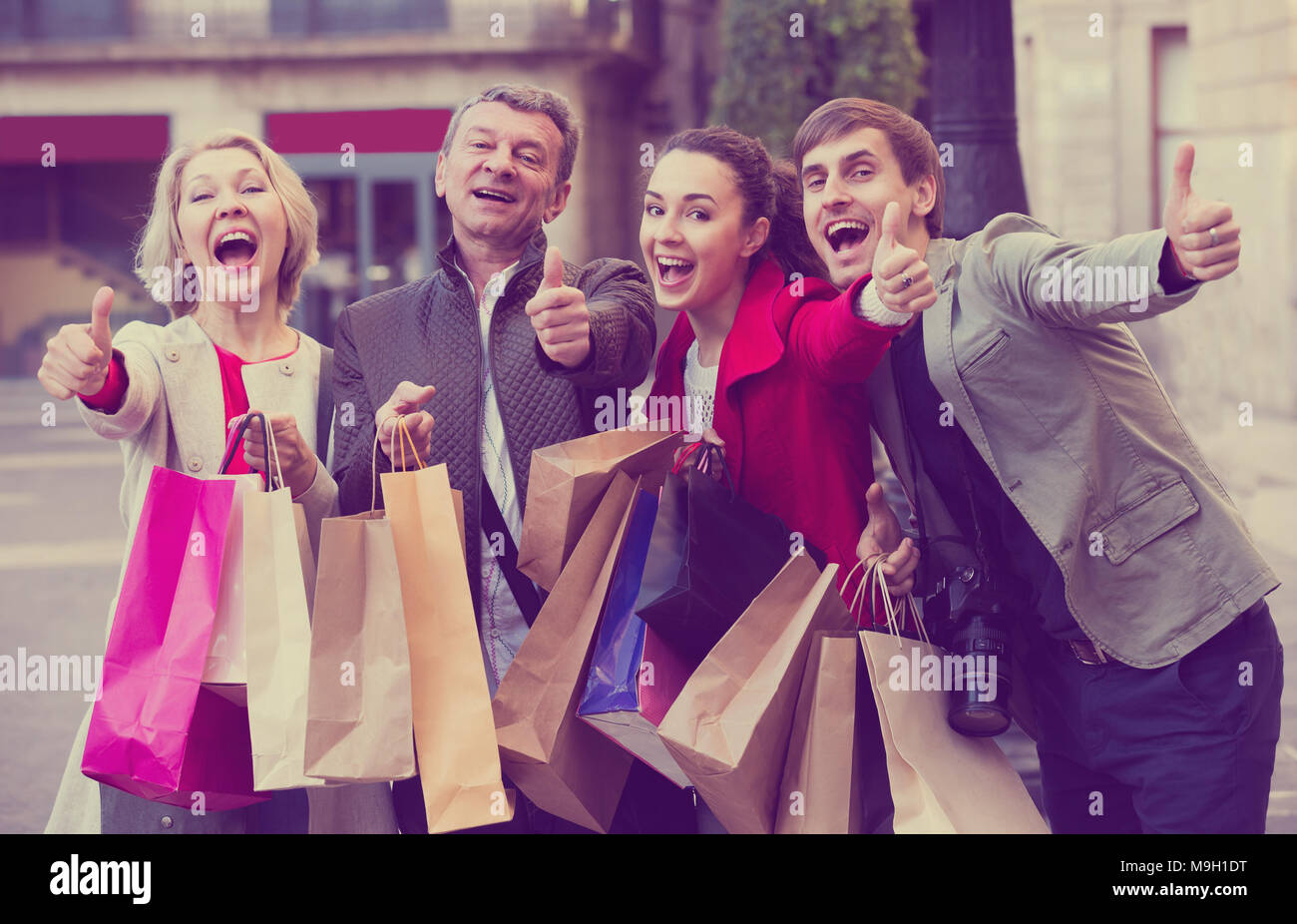 Happy family of four with shopping bags on city street Stock Photo - Alamy