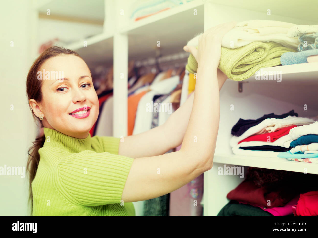 Smiling middle-aged female customer choosing apparel on shelves at ...