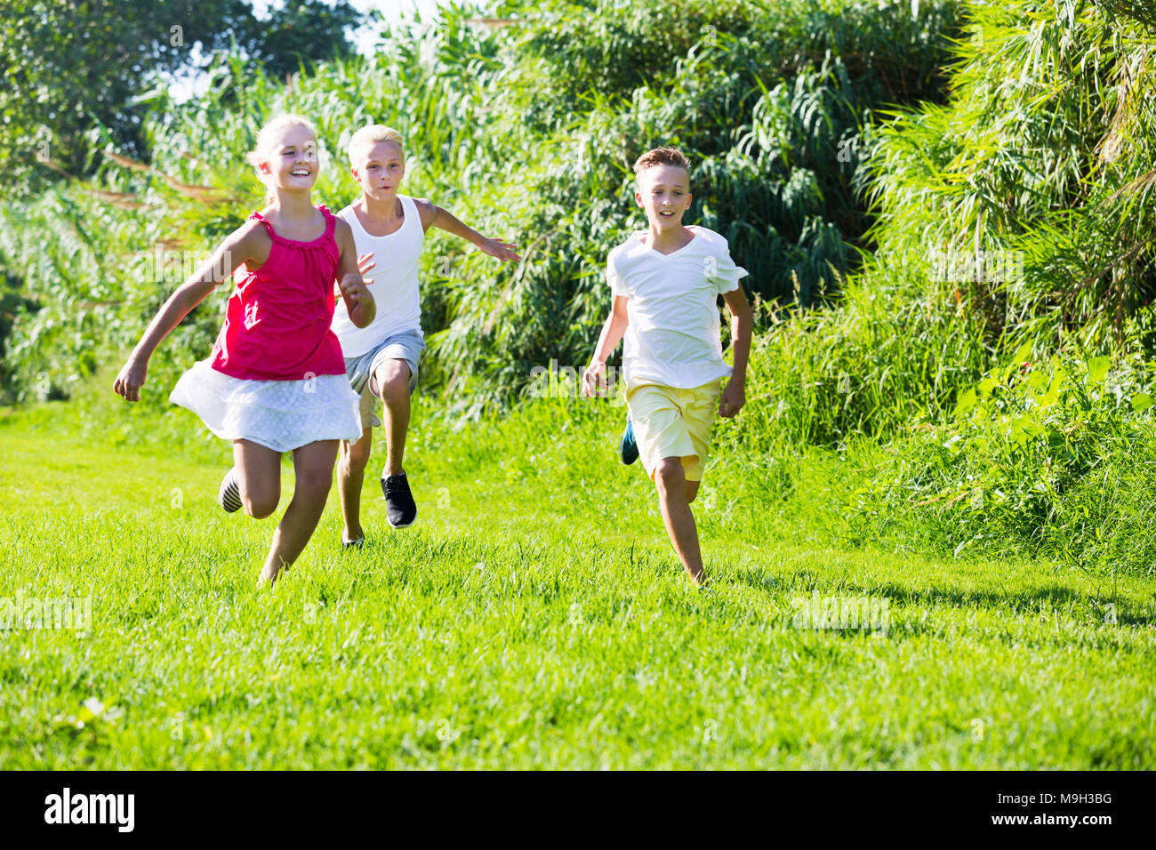 Three positive kids playing active games in summer park chasing each ...