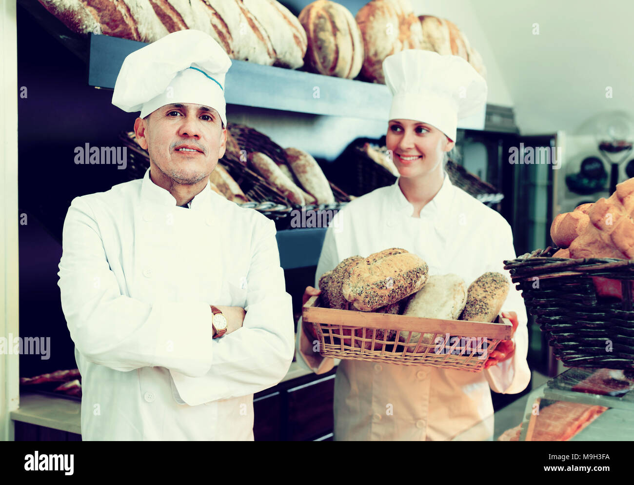 Positive male and female staff offering fresh baguettes and buns in ...