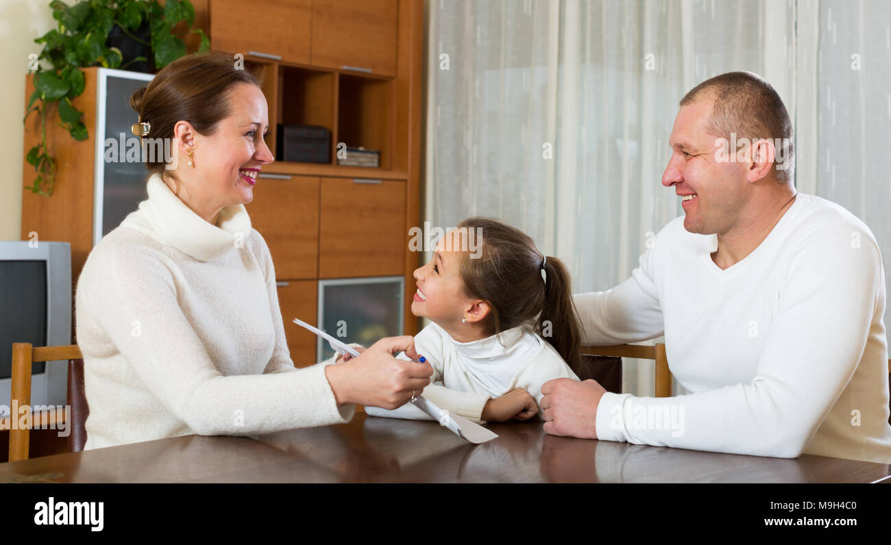 Happy parents and child with documents at the table in the living room ...