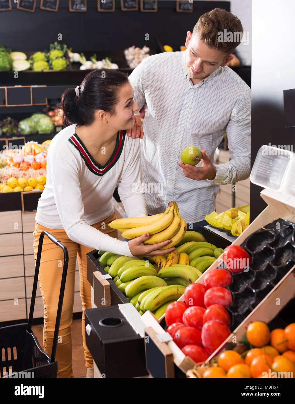 Young positive man and woman choosing fruits in grocery store. Focus on ...