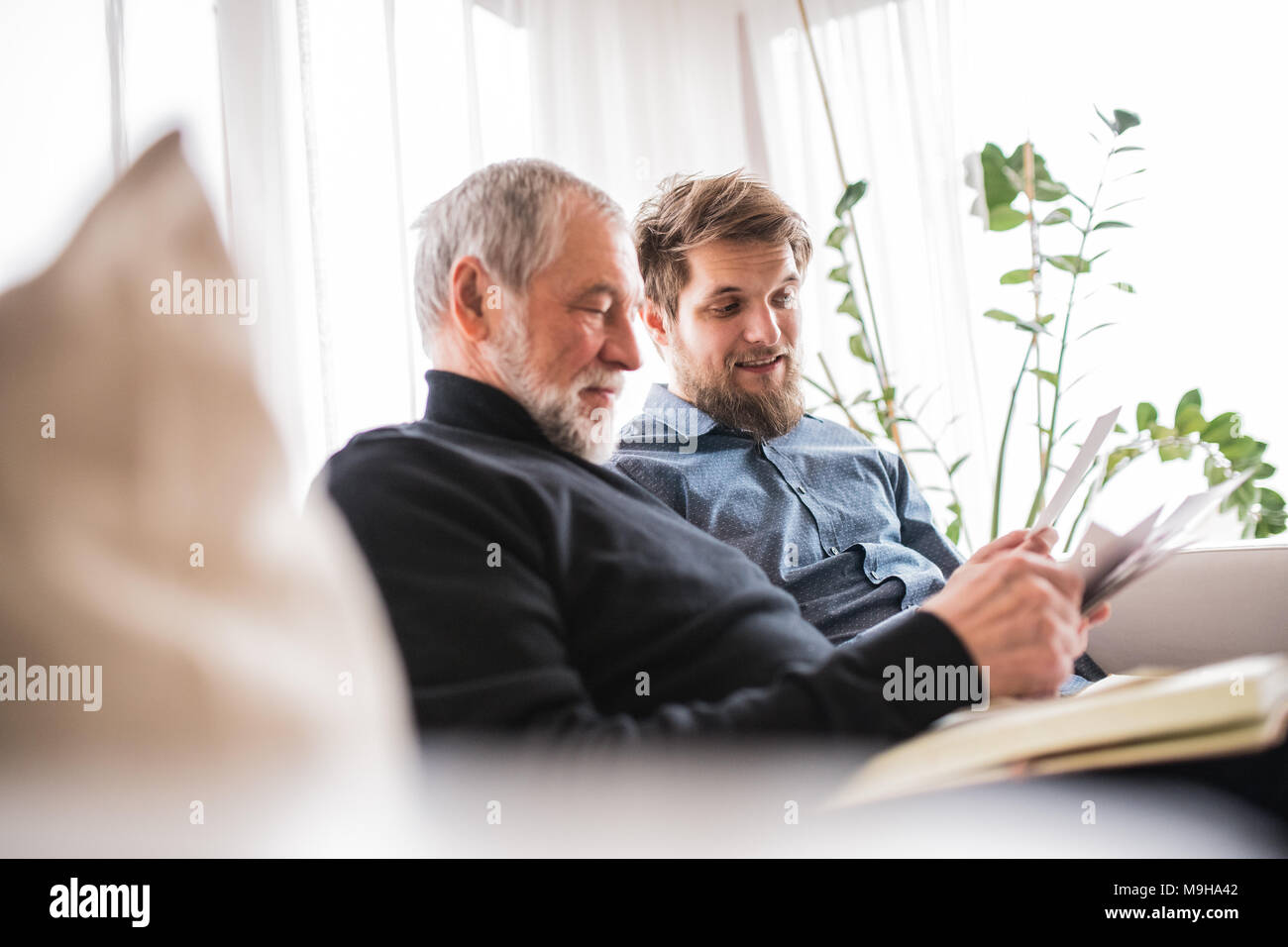 Hipster Son And His Senior Father At Home Looking At Old Photographs