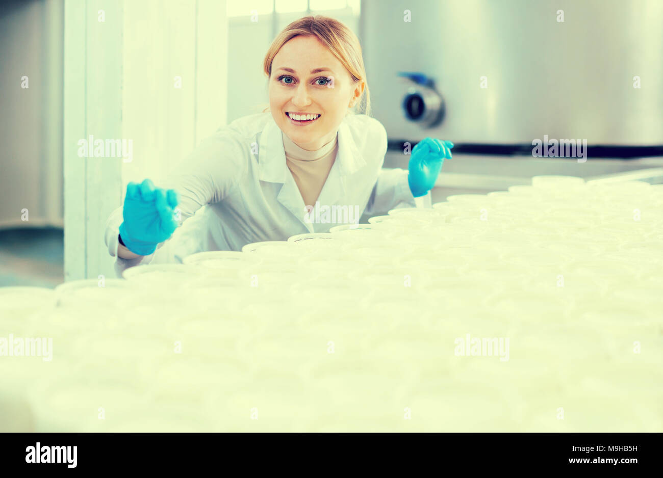 Happy woman wearing uniform showing cottage cheese production process ...