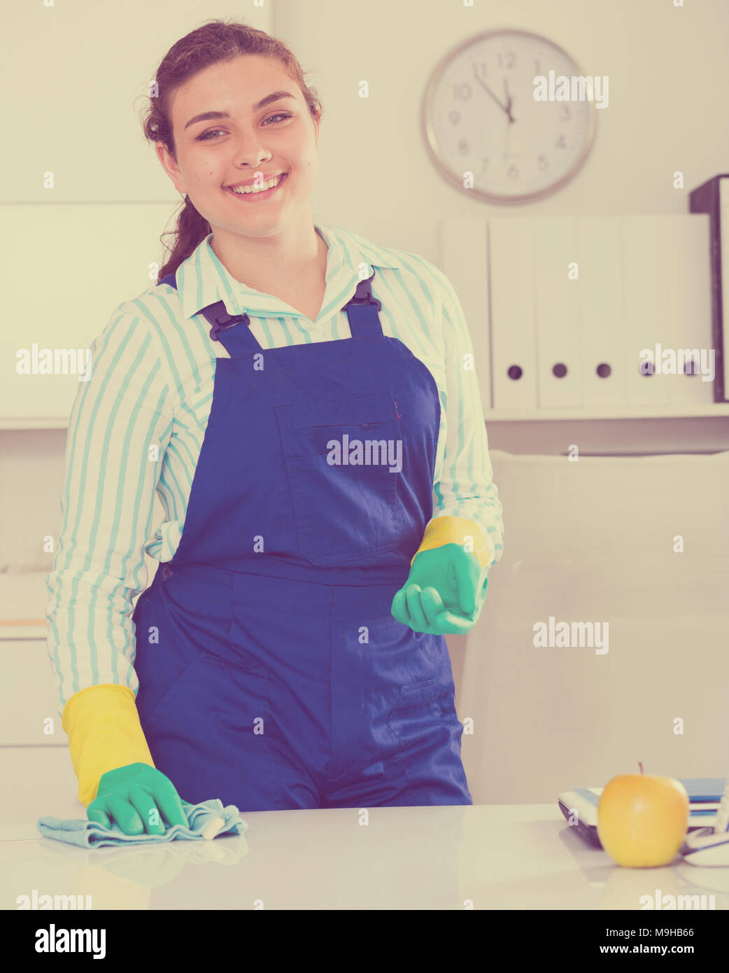 European female cleaner is cleaning dust from the desk in the office ...