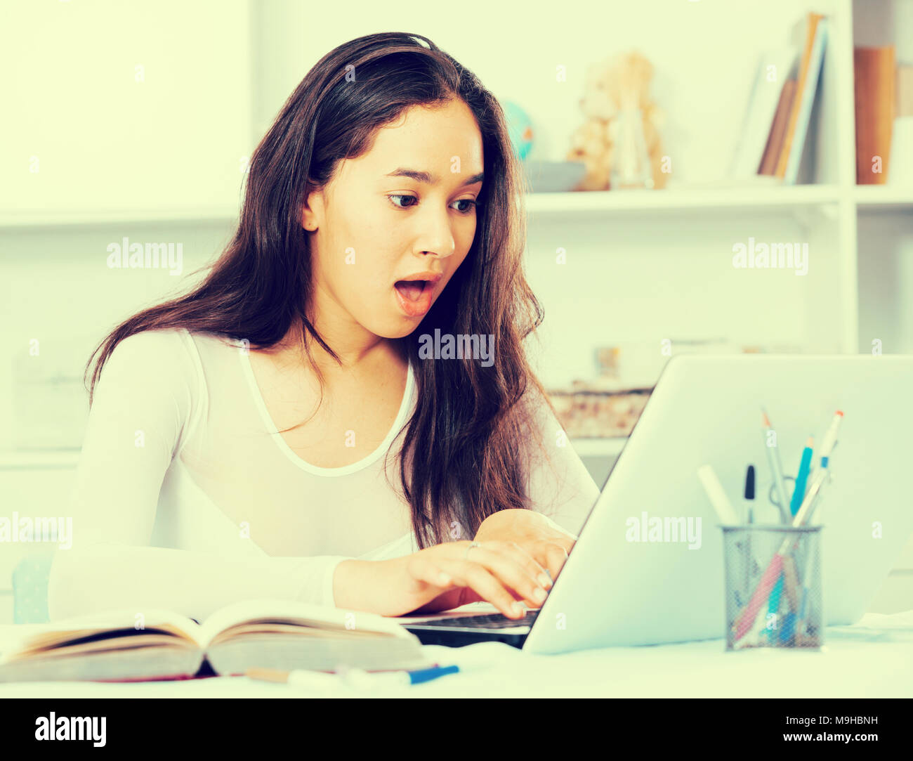 Young girl reading info in laptop and surprised indoors Stock Photo - Alamy