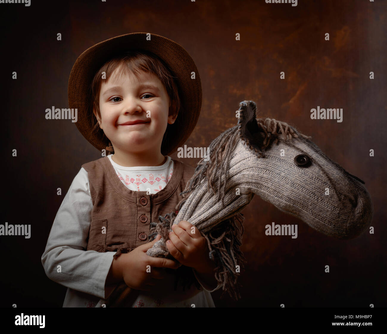 Cute little girl dressed like a cowboy playing with a homemade horse ...