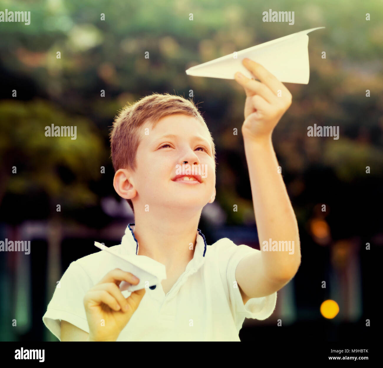 portrait of glad boy throwing paper airplanes in park on summer day ...
