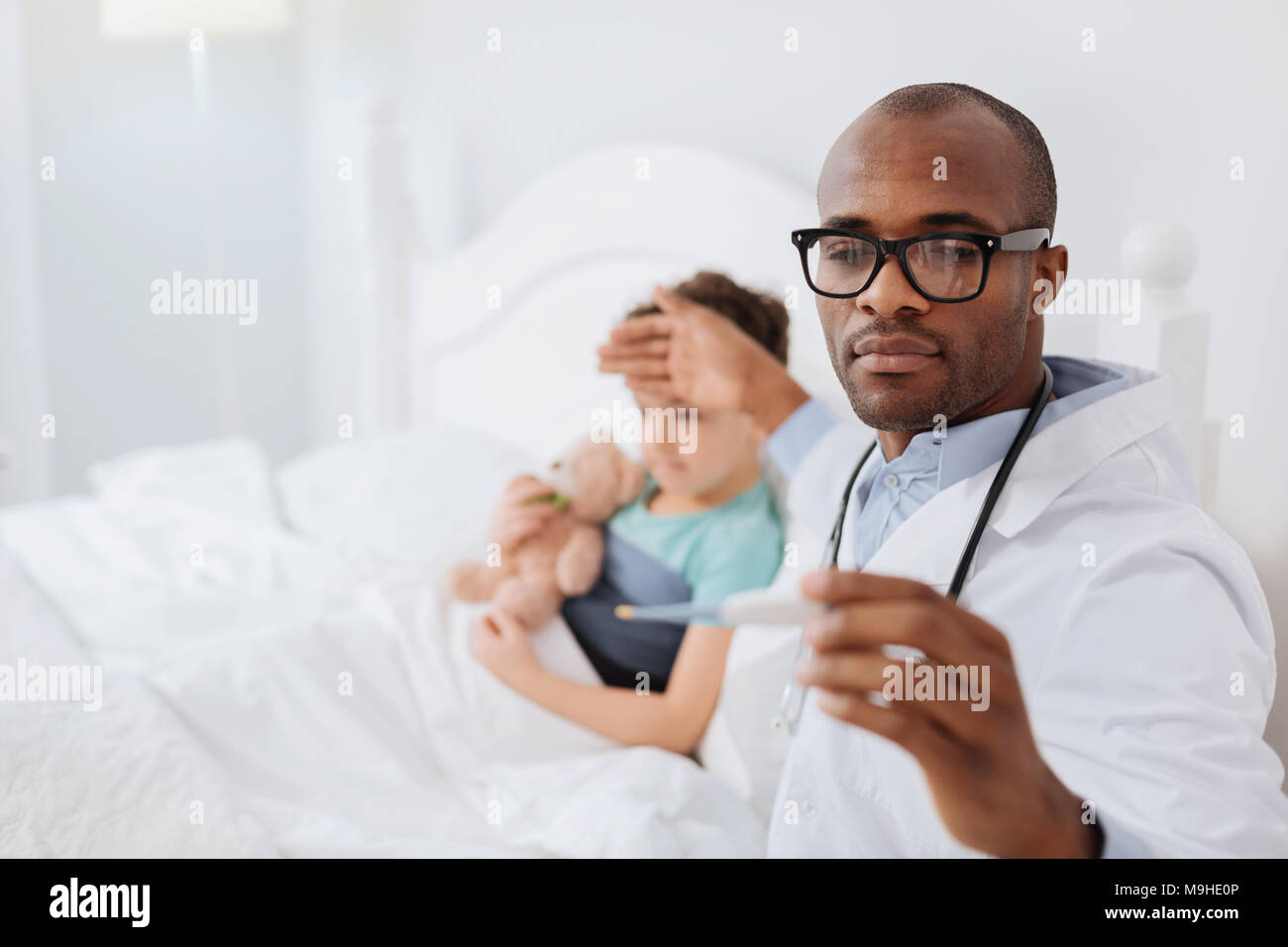 Positive male doctor defining boys temperature Stock Photo - Alamy