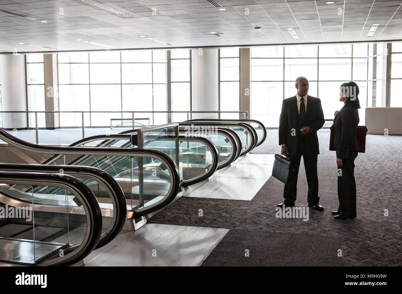 Two business people, man and woman standing in atrium of office ...