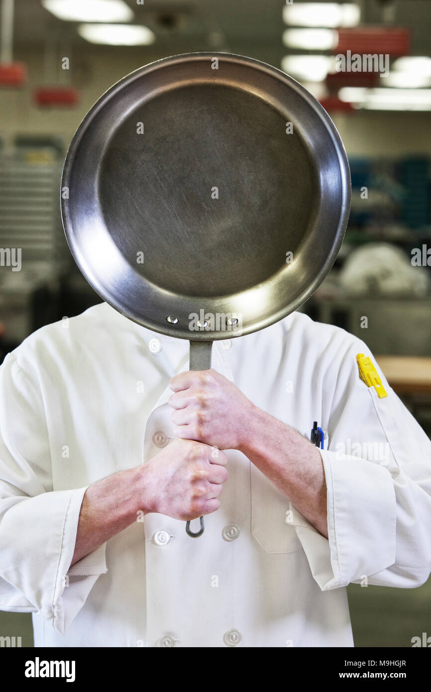 Close-up of a chef holding a sauté pan in front of his face in a ...