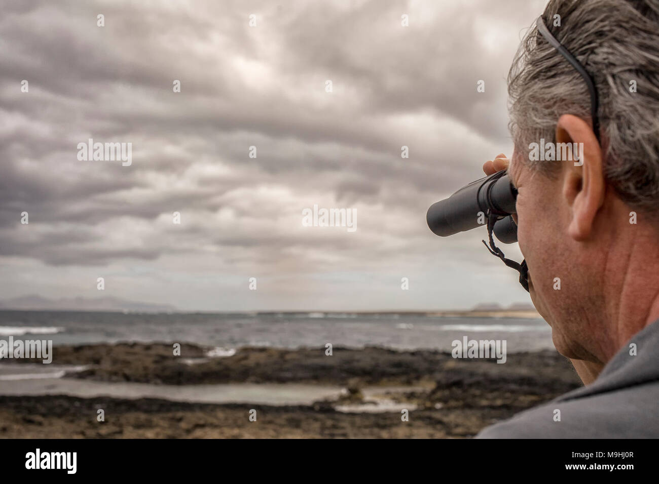 Man looking at horizon and ocean with binoculars Stock Photo - Alamy