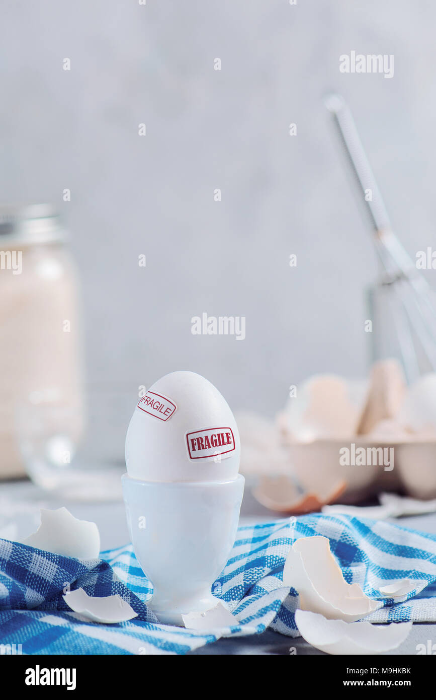 White egg in a porcelain egg stand with a red Fragile sign. High key ...