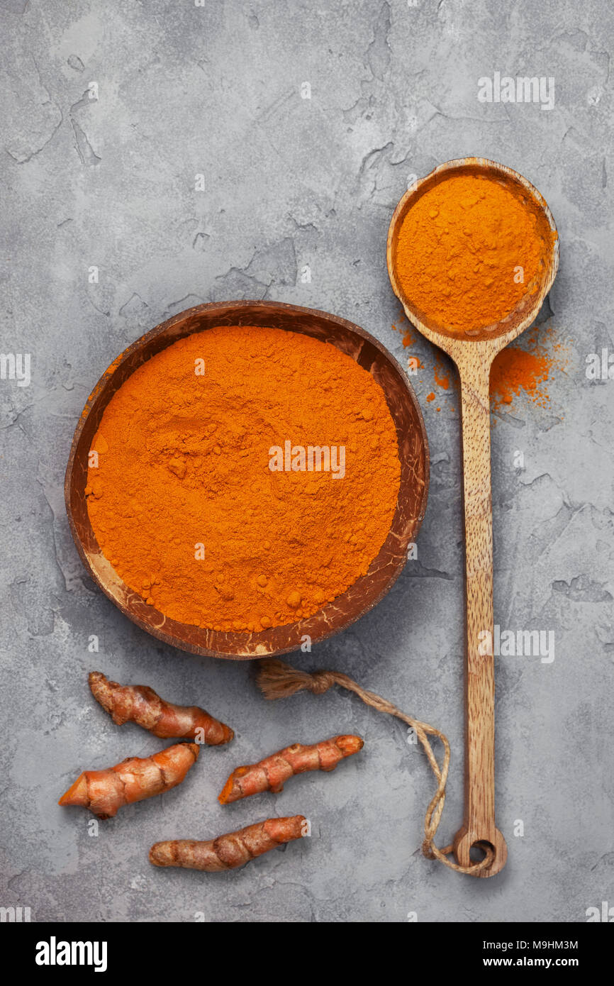 turmeric powder in a coconut bowl, turmeric roots on a gray concrete ...