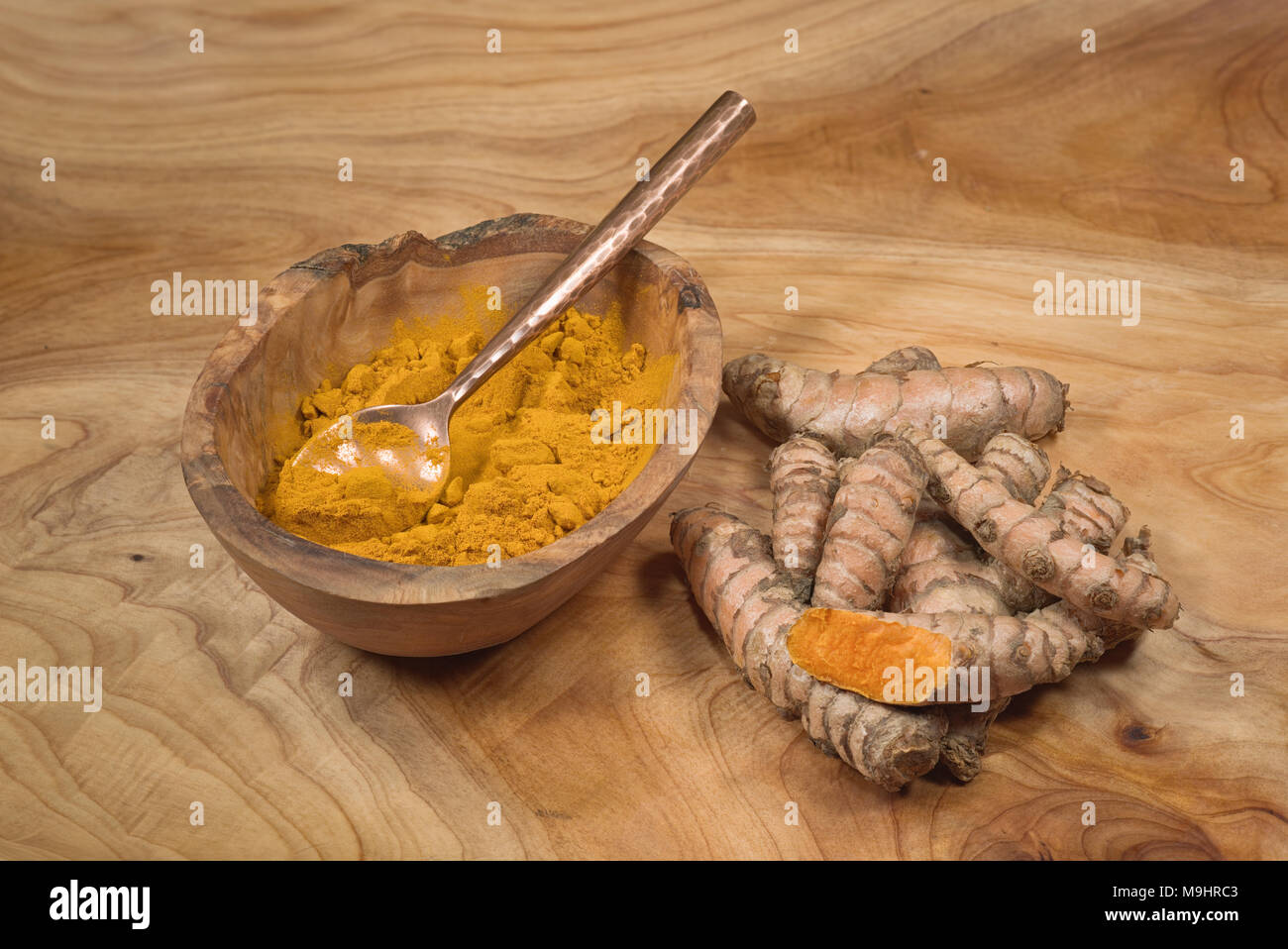 Turmeric root and powdered tumeric in wood bowl with copper spoon. One ...