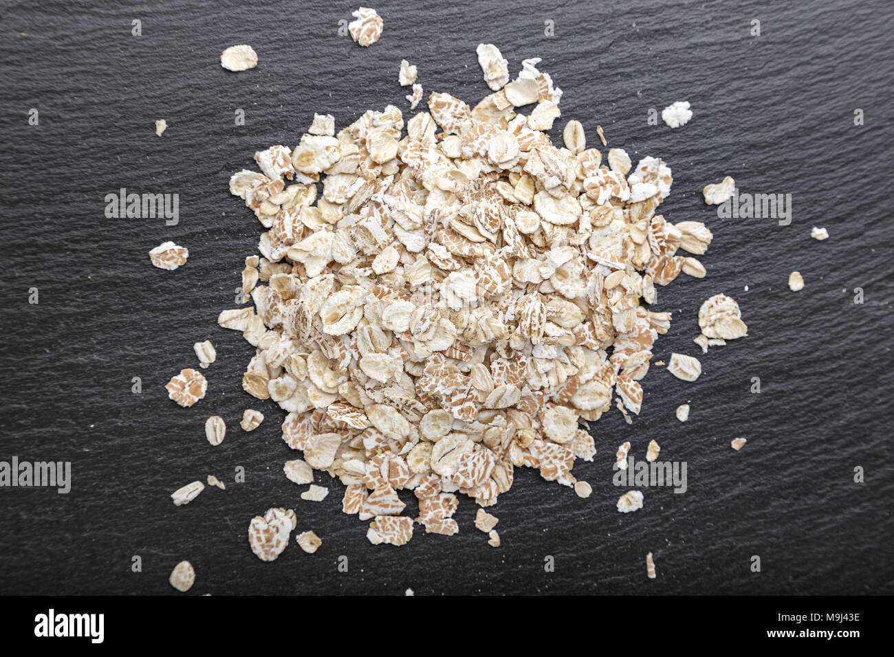 raw oatmeal is scattered on a black background, on slate blackboard ...