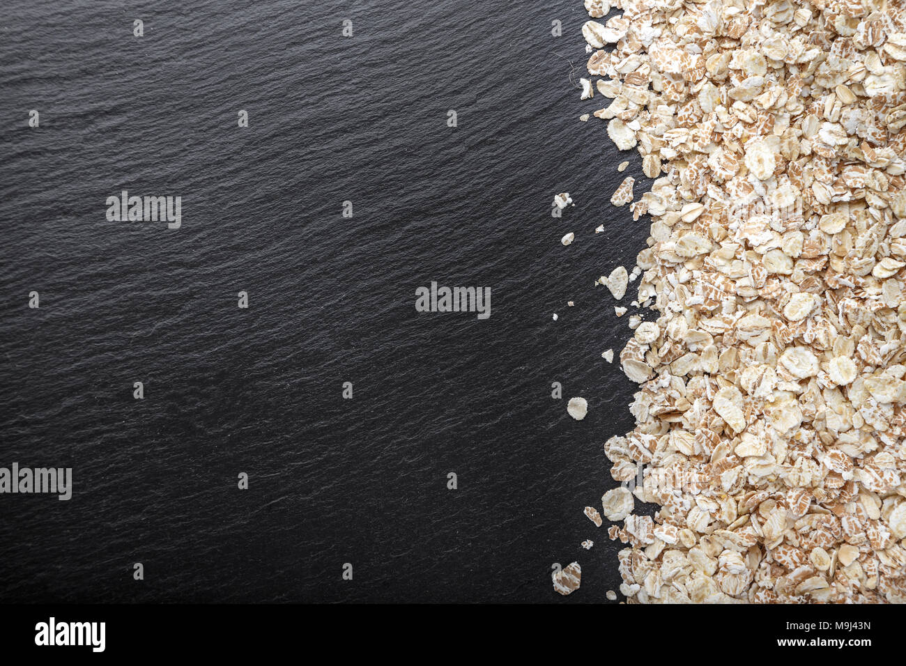raw oatmeal is scattered on a black background, on slate blackboard ...